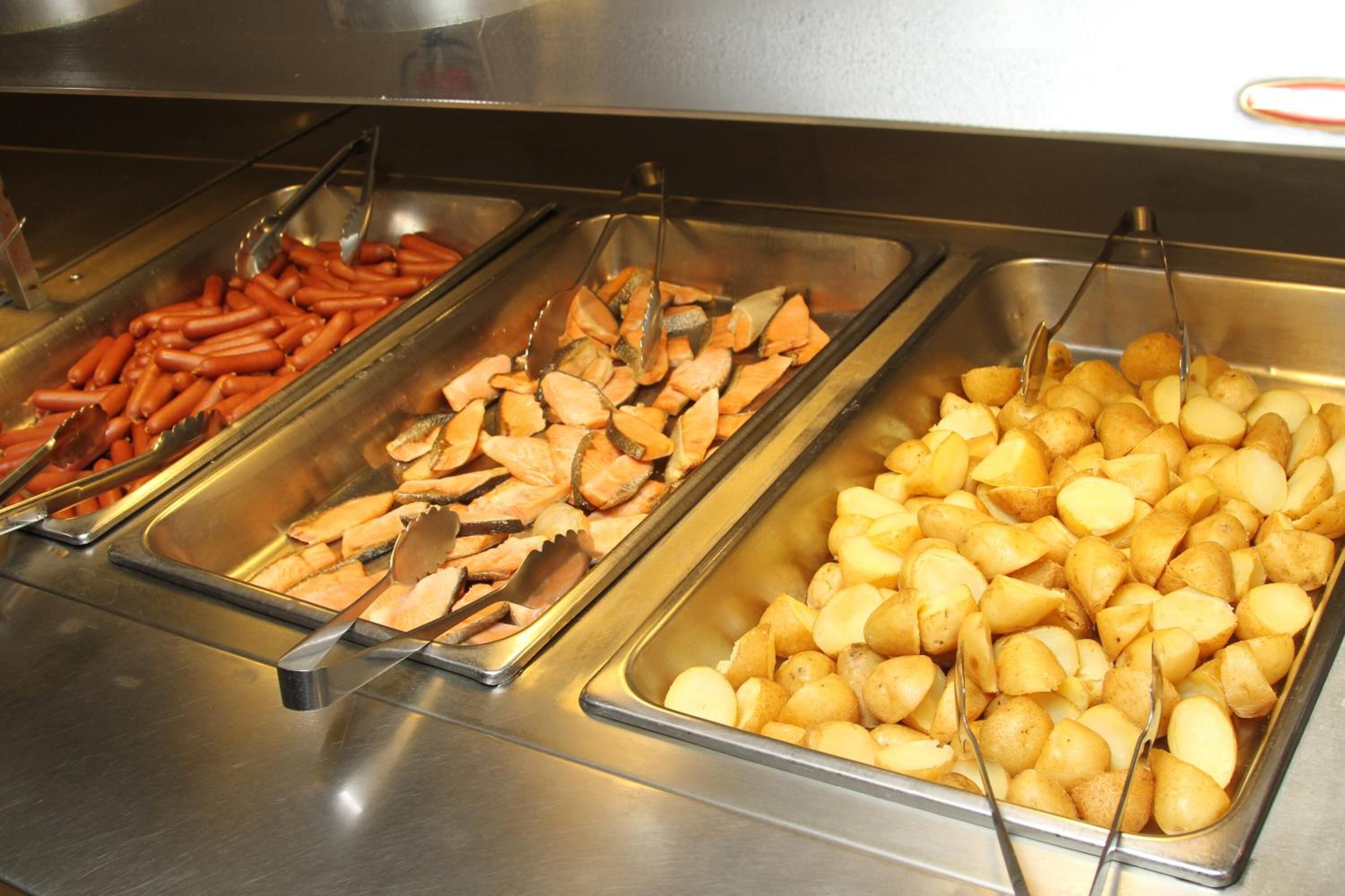 Buffet com bandejas de comida, incluindo cachorros-quentes, batata-doce e outros itens.
