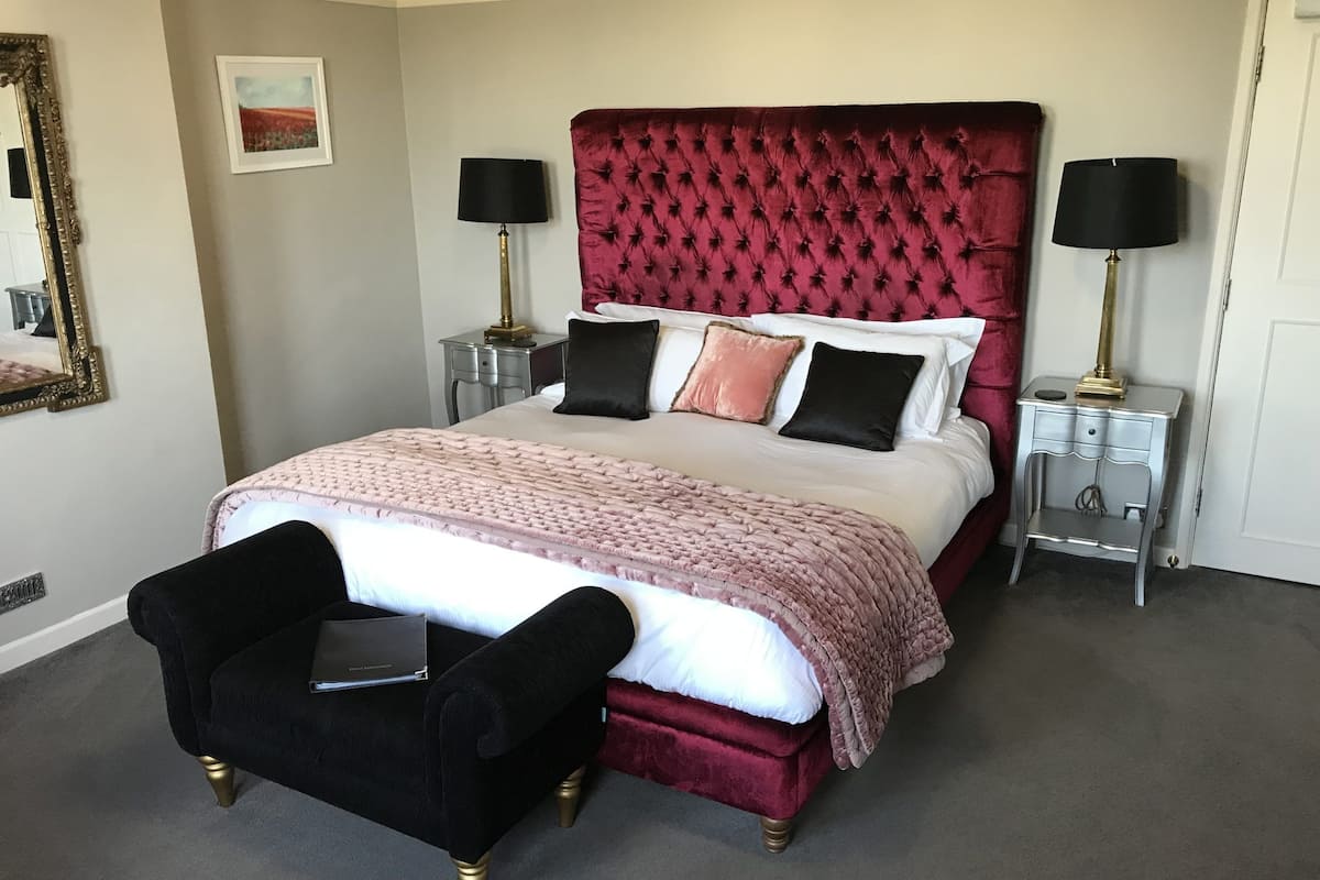Quarto com uma cama grande, duas mesas de cabeceira com abajures, uma poltrona preta e um espelho na parede.