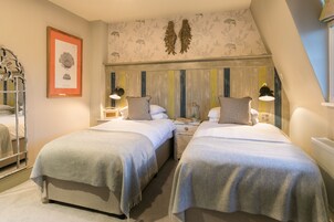 Quarto com duas camas, cabeceira de madeira, quadro emoldurado e espelho.