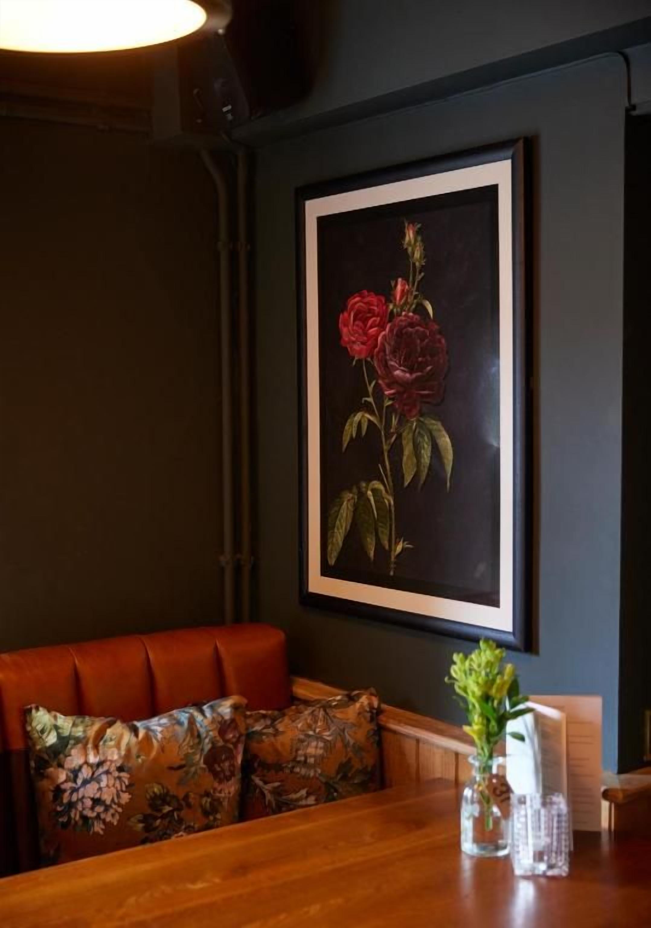 Uma área de refeições com uma mesa de madeira, um banco acolchoado e uma obra de arte floral emoldurada na parede.