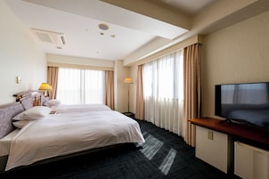 Quarto de hotel com cama, televisão, escrivaninha e radiador.