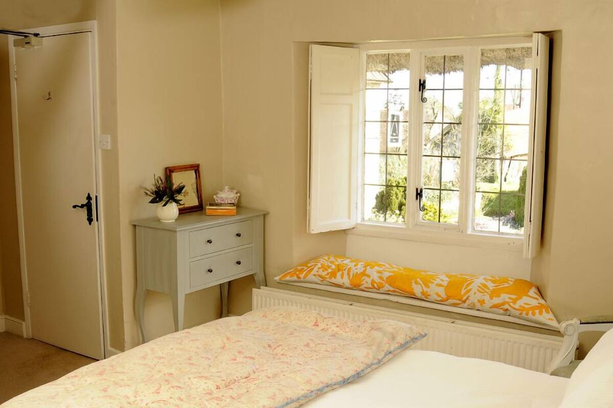 Um quarto com cama, cômoda, janela com vista para o verde e porta.
