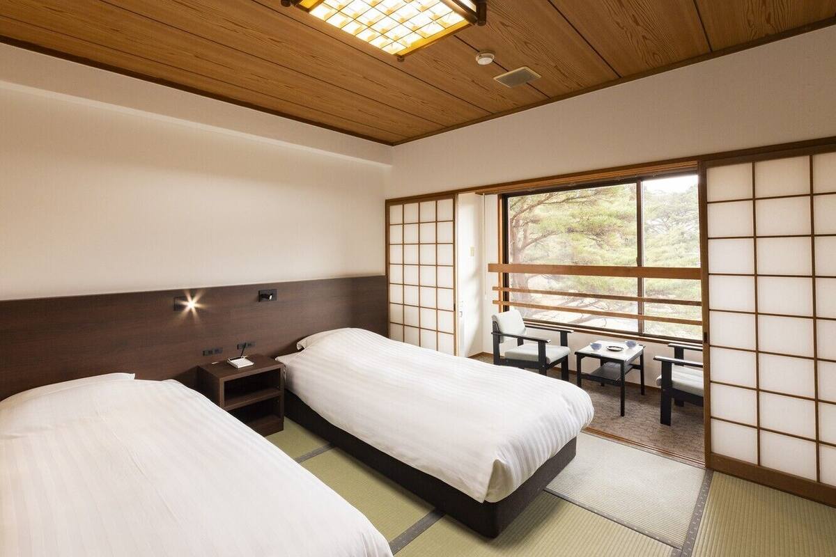 Quarto japonês tradicional com tatames, duas camas, uma mesinha e vista por meio de biombos shoji.