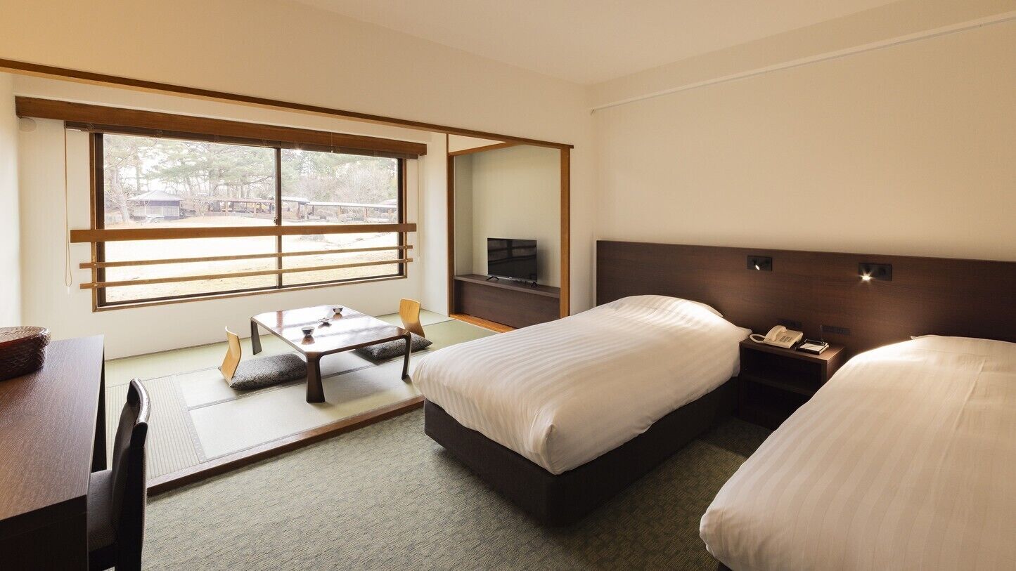 Quarto de hotel com duas camas, televisão, escrivaninha e janela com persianas.
