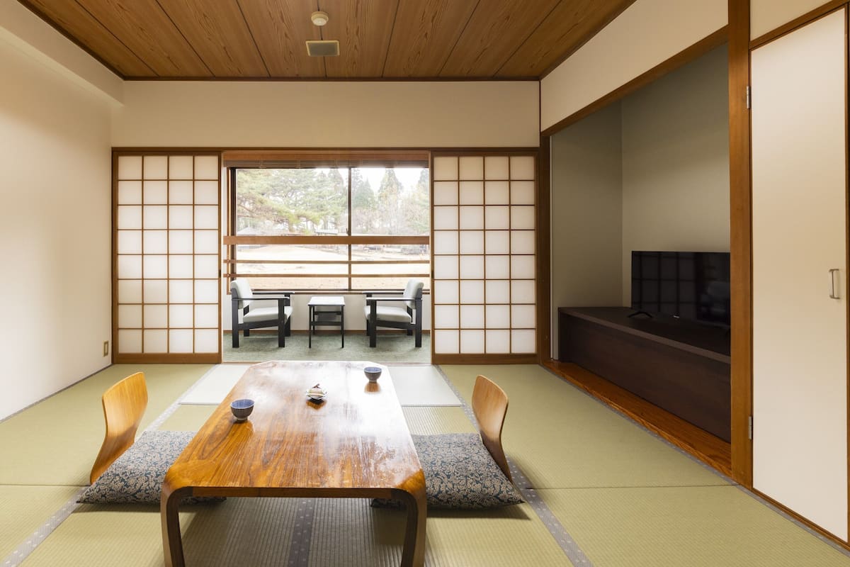 Um quarto japonês tradicional com tatames, uma mesa de madeira baixa e portas deslizantes.