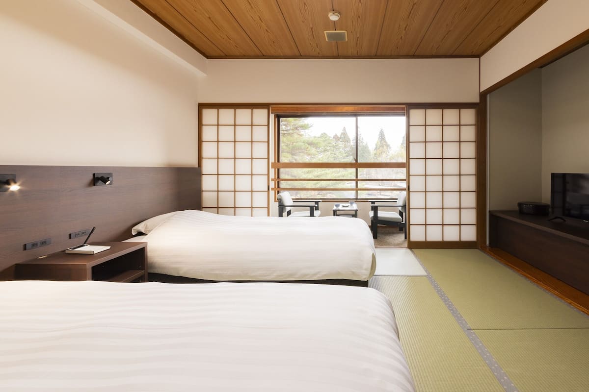 Quarto de hotel com duas camas, uma televisão, uma escrivaninha e vista através de um ecrã shoji.