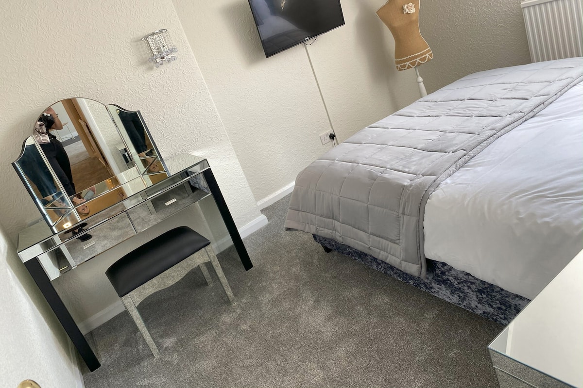 Quarto com cama, penteadeira, espelho, televisão e um manequim.