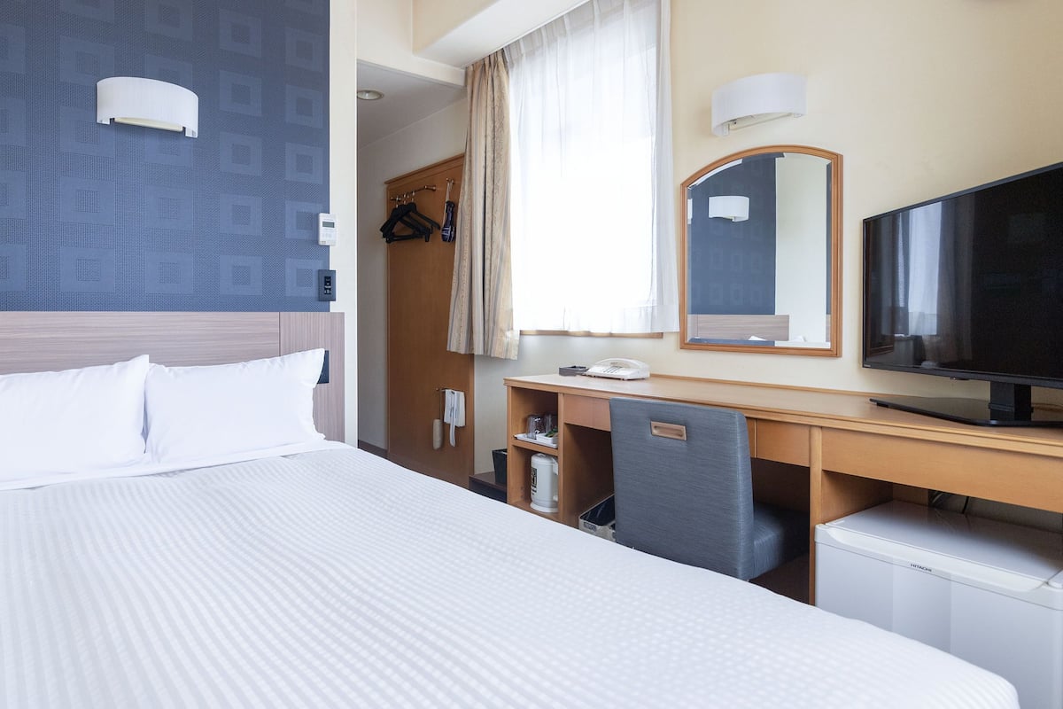 Quarto de hotel com uma cama grande, uma escrivaninha com cadeira, televisão e espelho.