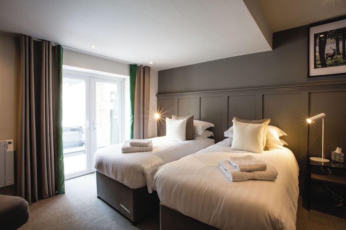 Quarto de hotel com duas camas, uma janela grande e um quadro emoldurado na parede.