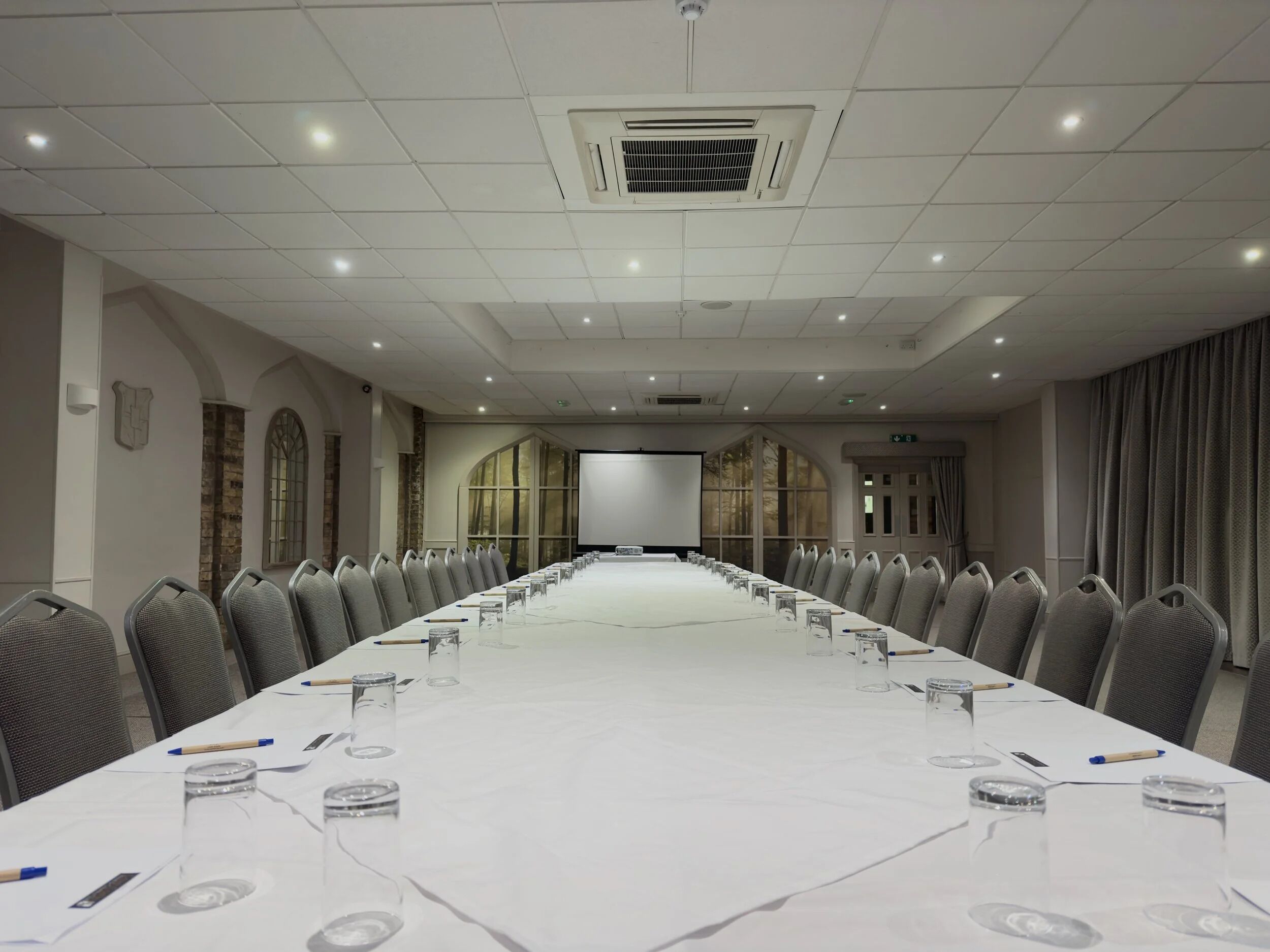 Uma sala de conferência com uma mesa comprida, cadeiras e uma tela de projeção.