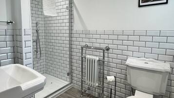 Casa de banho com chuveiro, lavatório, sanita e radiador.
