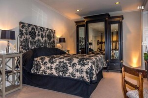 Quarto com uma cama grande, mesa de cabeceira, escrivaninha e guarda-roupa com espelho.