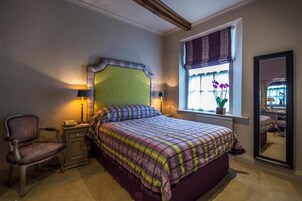 Quarto com cama, cadeira, mesa de cabeceira, janela com cortinas e espelho.