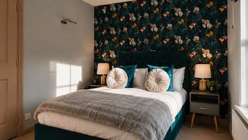 Quarto com cama, duas mesinhas de cabeceira, um criado-mudo, uma janela e papel de parede floral.