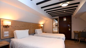 Quarto de hotel com duas camas, cabeceira de madeira com iluminação embutida, uma escrivaninha com cadeira e uma escada para outro andar.