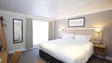 Quarto de hotel com uma cama grande, mesas de cabeceira, um espelho e uma janela com cortinas.