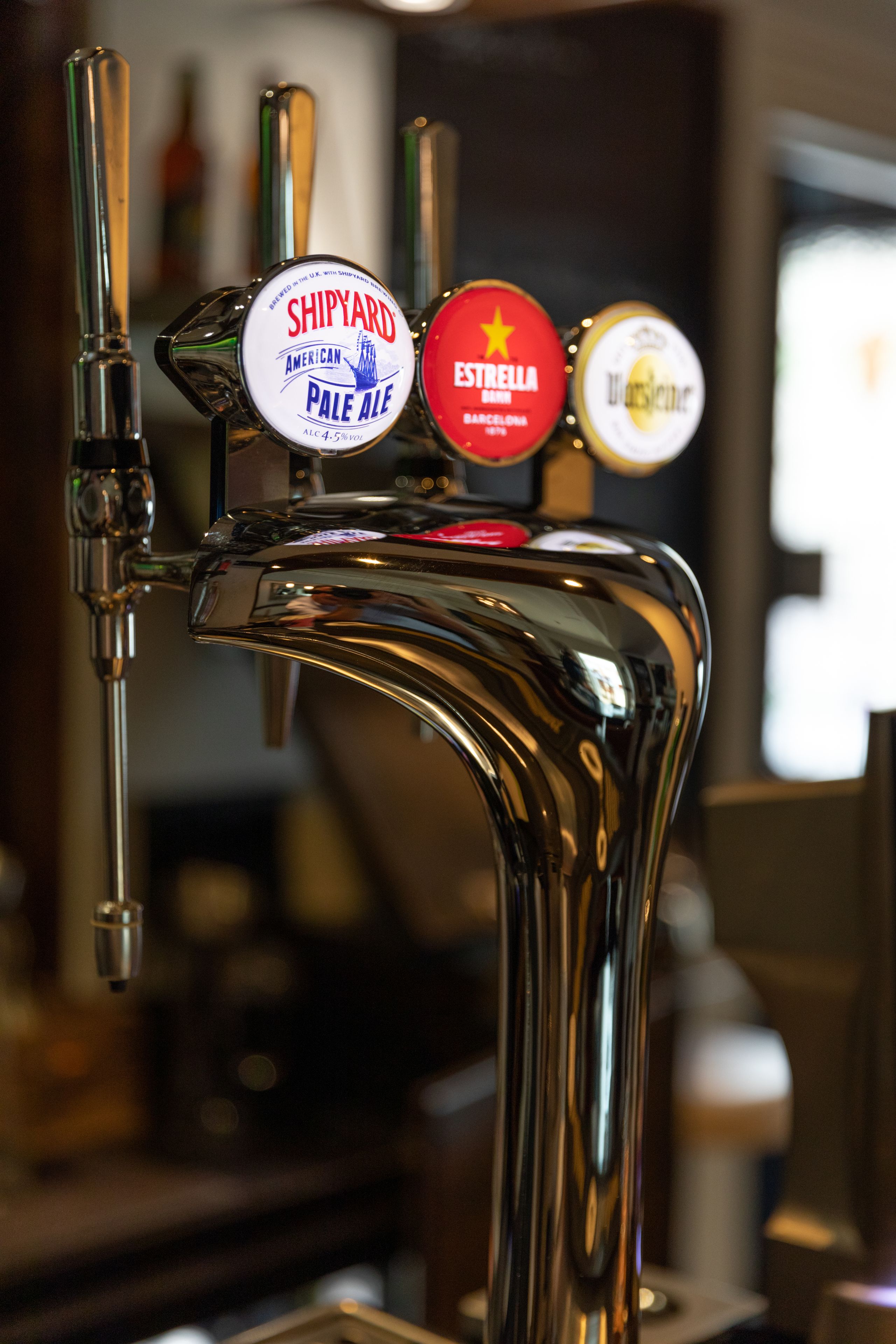 Uma torneira com três rótulos de cerveja: Shipyard Pale Ale, Estrella Bar e Basque.