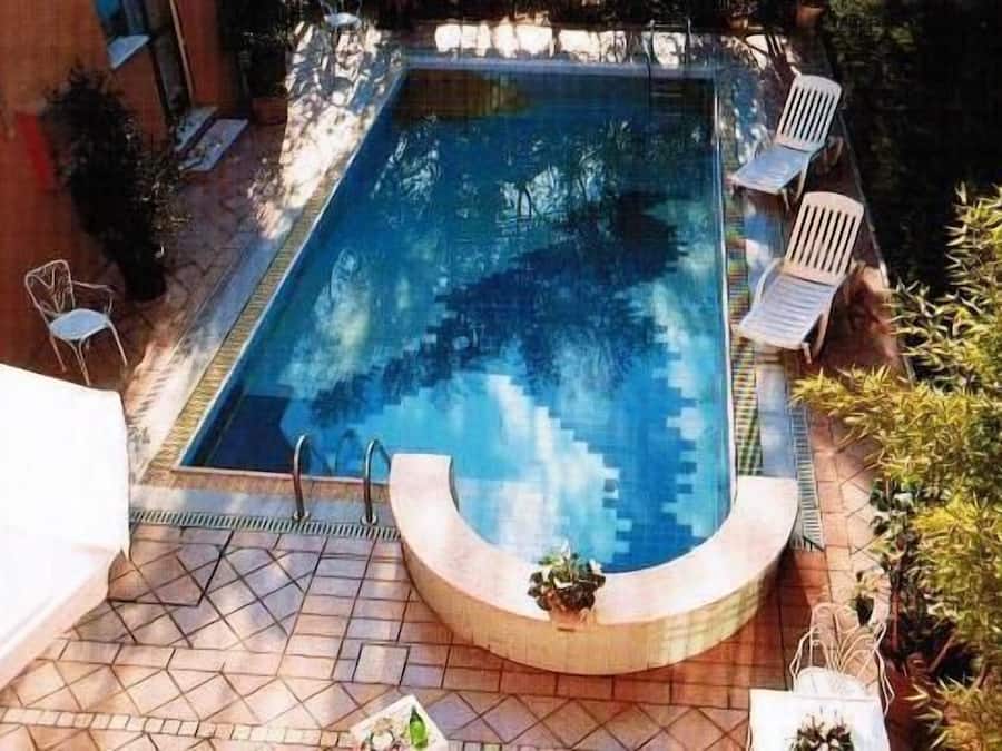 Piscina retangular com borda curva, ladeada por um pátio revestido de azulejos.