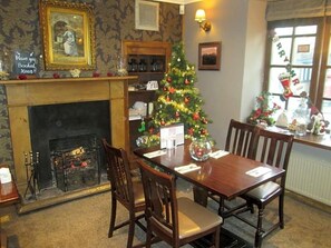 Uma área de refeições com mesa e cadeiras de madeira, uma árvore de Natal e uma lareira.