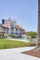 Um edifício grande, com vários andares, uma torre imponente, piscina e um gramado bem cuidado.
