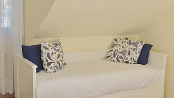 Quarto com cama branca, duas almofadas estampadas e cabeceira branca.