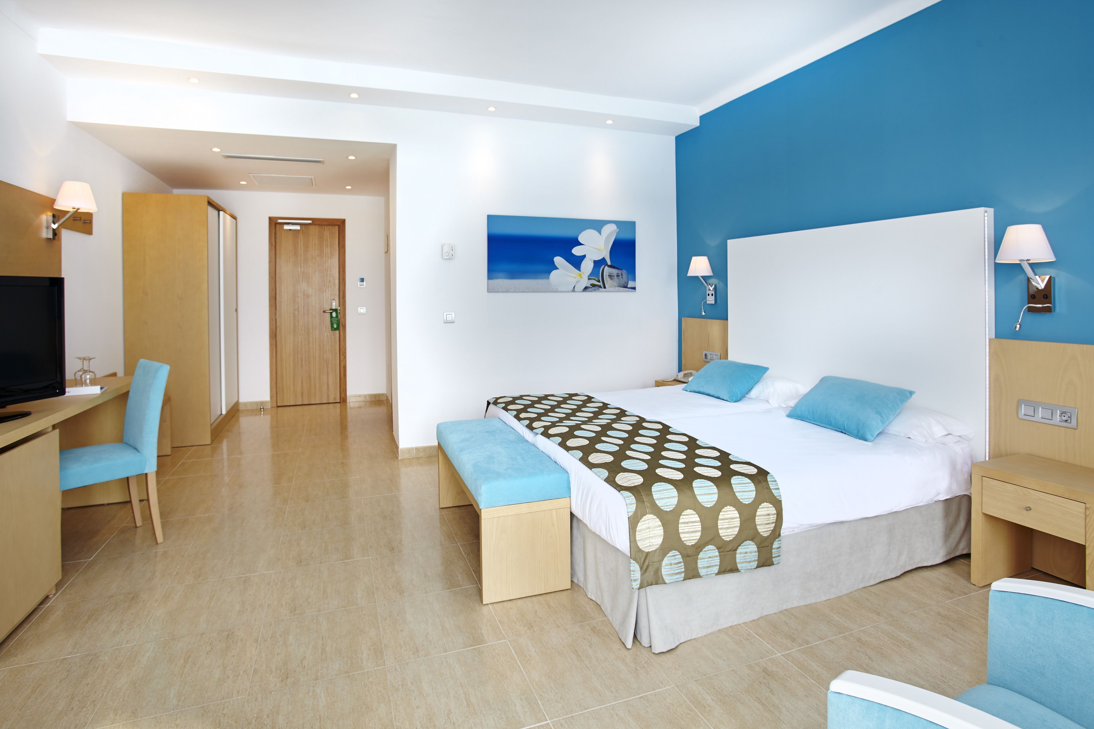 Quarto de hotel moderno com uma cama grande, uma escrivaninha, uma cadeira e uma televisão.