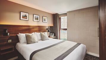Quarto de hotel com uma cama grande, cabeceira de madeira, mesa de cabeceira com abajur e três quadros na parede.