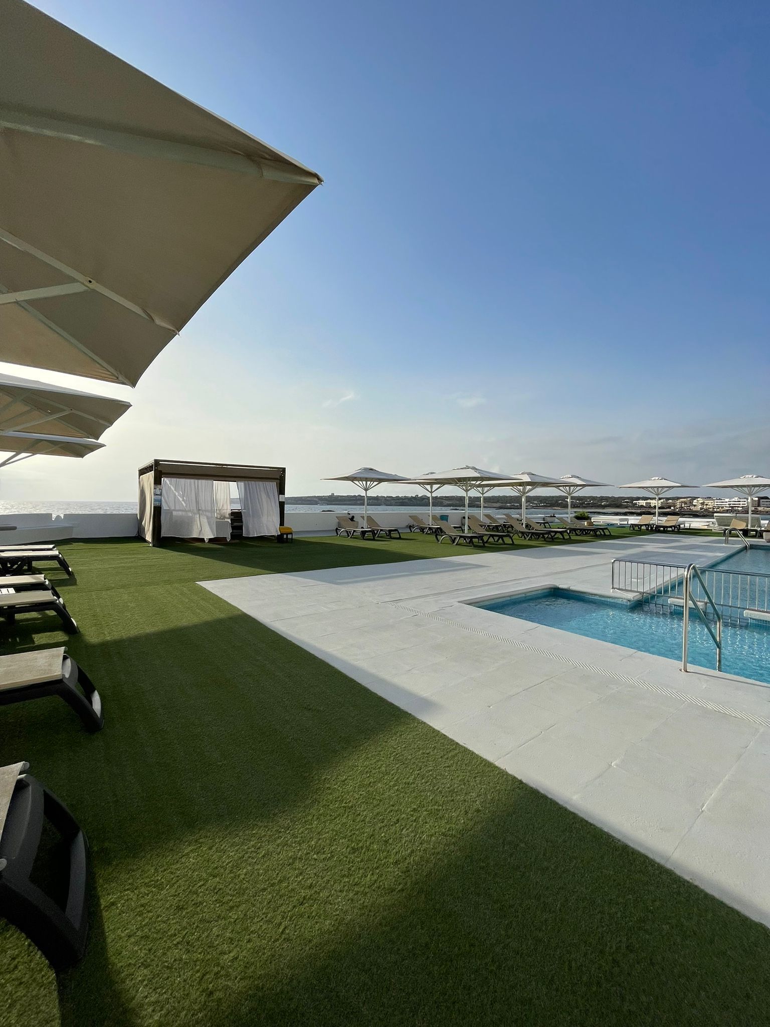 Uma área de piscina no terraço com grama sintética, espreguiçadeiras e guarda-sóis.