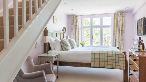 Quarto com cama grande, cadeira, cômoda e janela com cortinas.