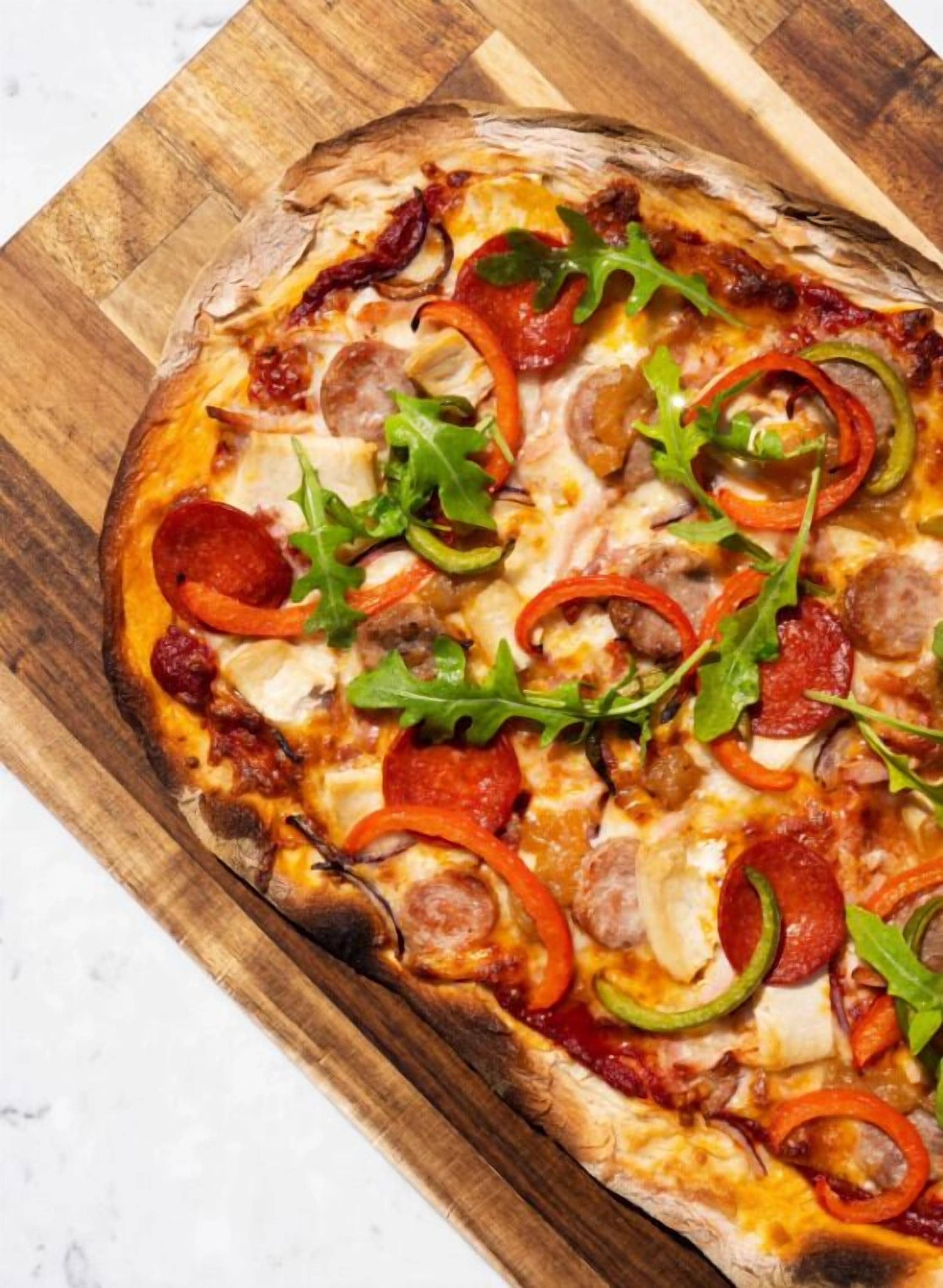 Uma pizza com diversos ingredientes sobre uma tábua de madeira.