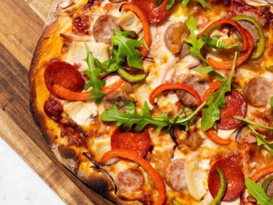 Uma pizza com diversos ingredientes sobre uma tábua de madeira.