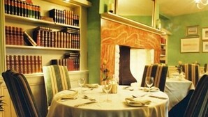 Uma sala de jantar com uma mesa redonda posta para quatro pessoas, rodeada por cadeiras estofadas.
