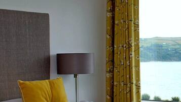 Quarto com cama, mesa de cabeceira, abajur e janela com cortinas.