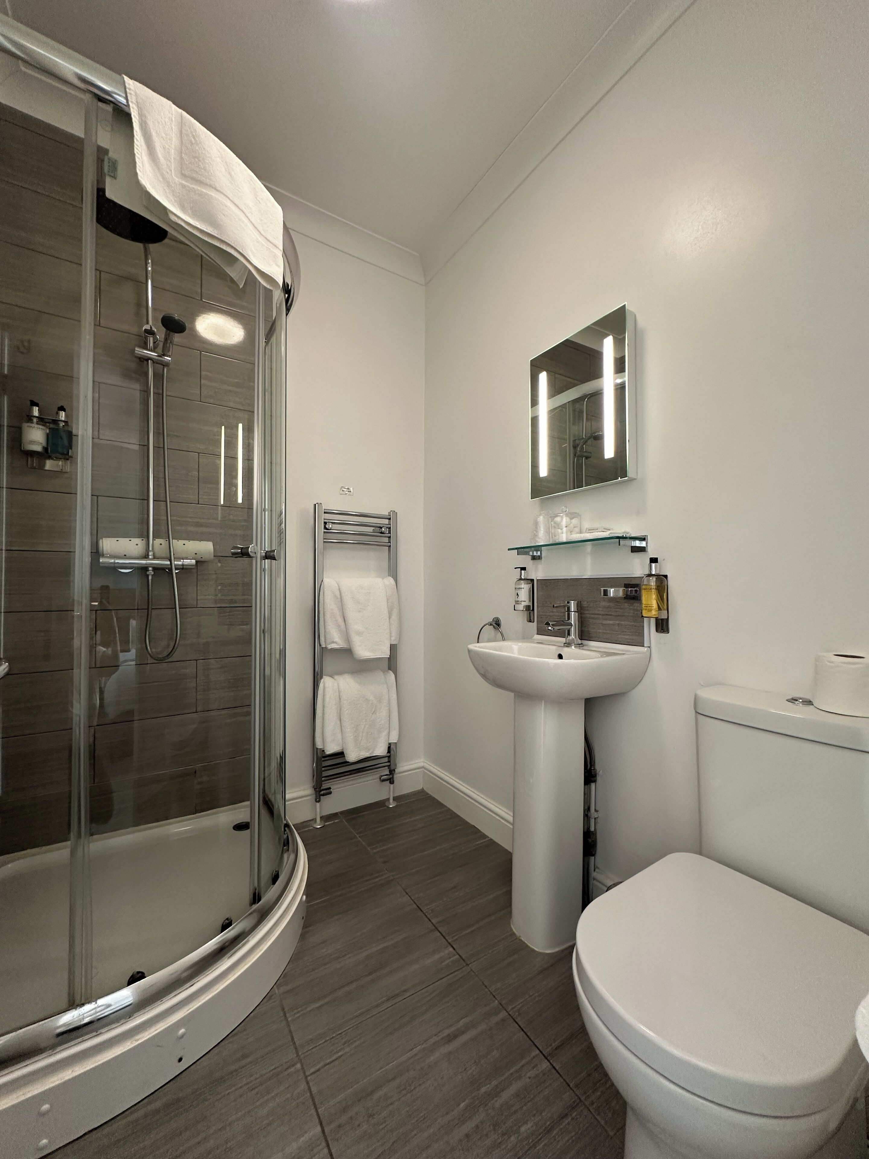 Uma casa de banho moderna com chuveiro envidraçado, sanita branca e lavatório com espelho em cima.