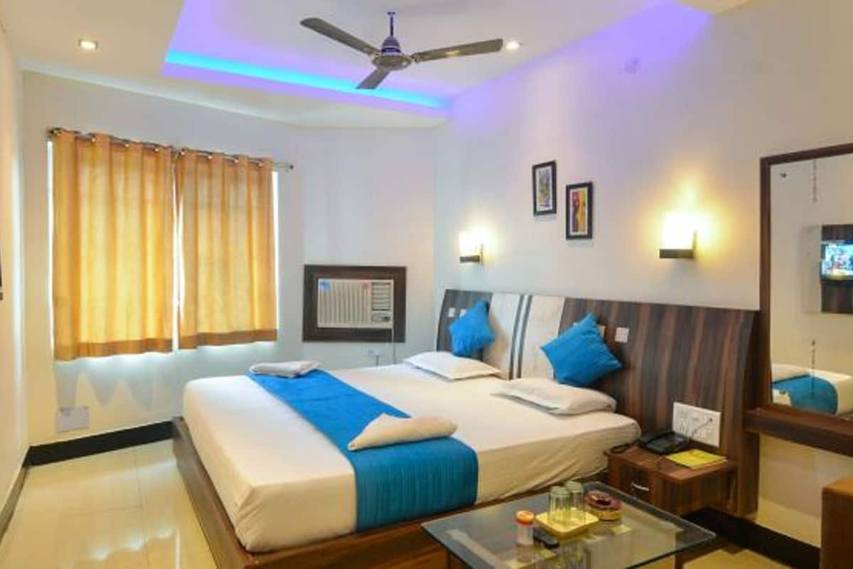 Quarto de hotel com uma cama grande, ventoinha no teto, televisão de tela plana, mesa de cabeceira e espelho de banheiro.