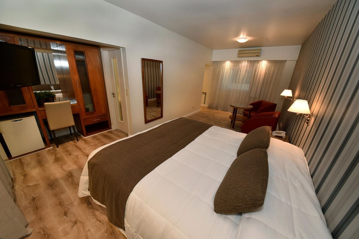 Quarto de hotel com uma cama grande, uma mesa de trabalho com cadeira, televisão e espelho.