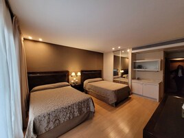 Quarto de hotel com duas camas, uma televisão, um espelho e um guarda-roupa.