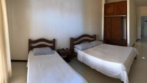 Quarto com duas camas de solteiro, cabeceiras de madeira, um guarda-roupa e corredor que dá para outro quarto.