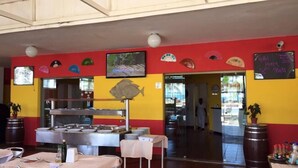 Interior de restaurante com esquema de cores vermelho e amarelo, decoração de peixe, um peixe grande em suporte e um cardápio em lousa.