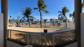Uma varanda com vista para uma praia, palmeiras e um céu claro.