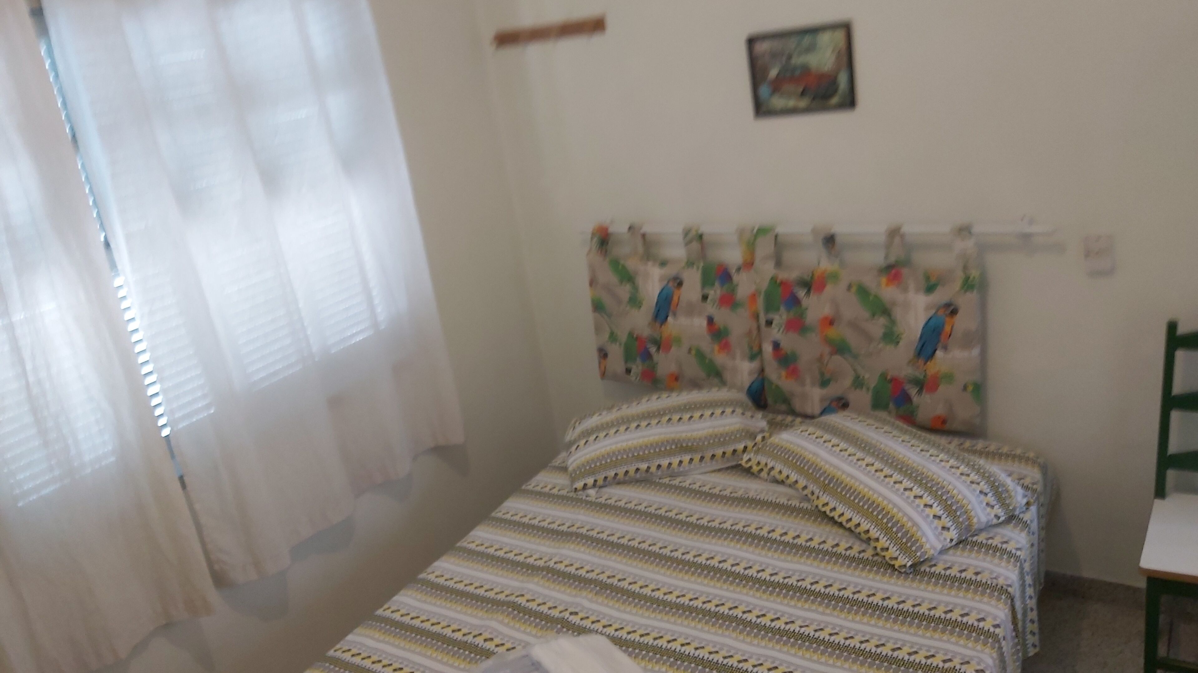 Quarto com cama, cortinas, um quadro na parede e uma cadeira.