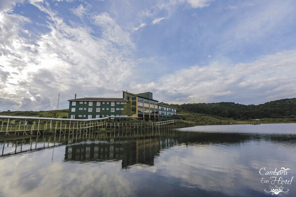 Um hotel com design moderno, um cais que se estende por um lago calmo, rodeado por vegetação.
