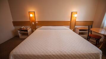 Quarto de hotel com uma cama grande, mesas de cabeceira, escrivaninha e uma cadeira.