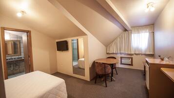 Quarto de hotel com cama, escrivaninha, cadeira, mesa pequena, espelho, janela com cortinas e televisão.