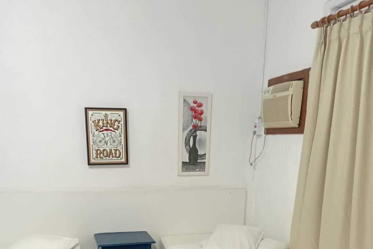 Quarto com duas camas, uma mesinha, ar-condicionado fixado na parede e duas fotos emolduradas.