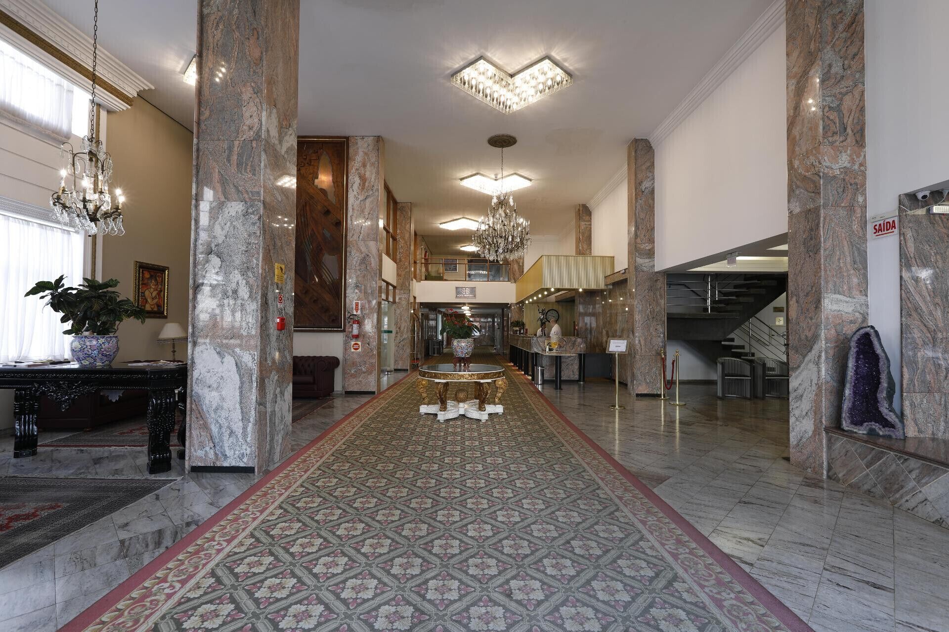 Um hall imponente com colunas de mármore, carpete estampado e lustres.