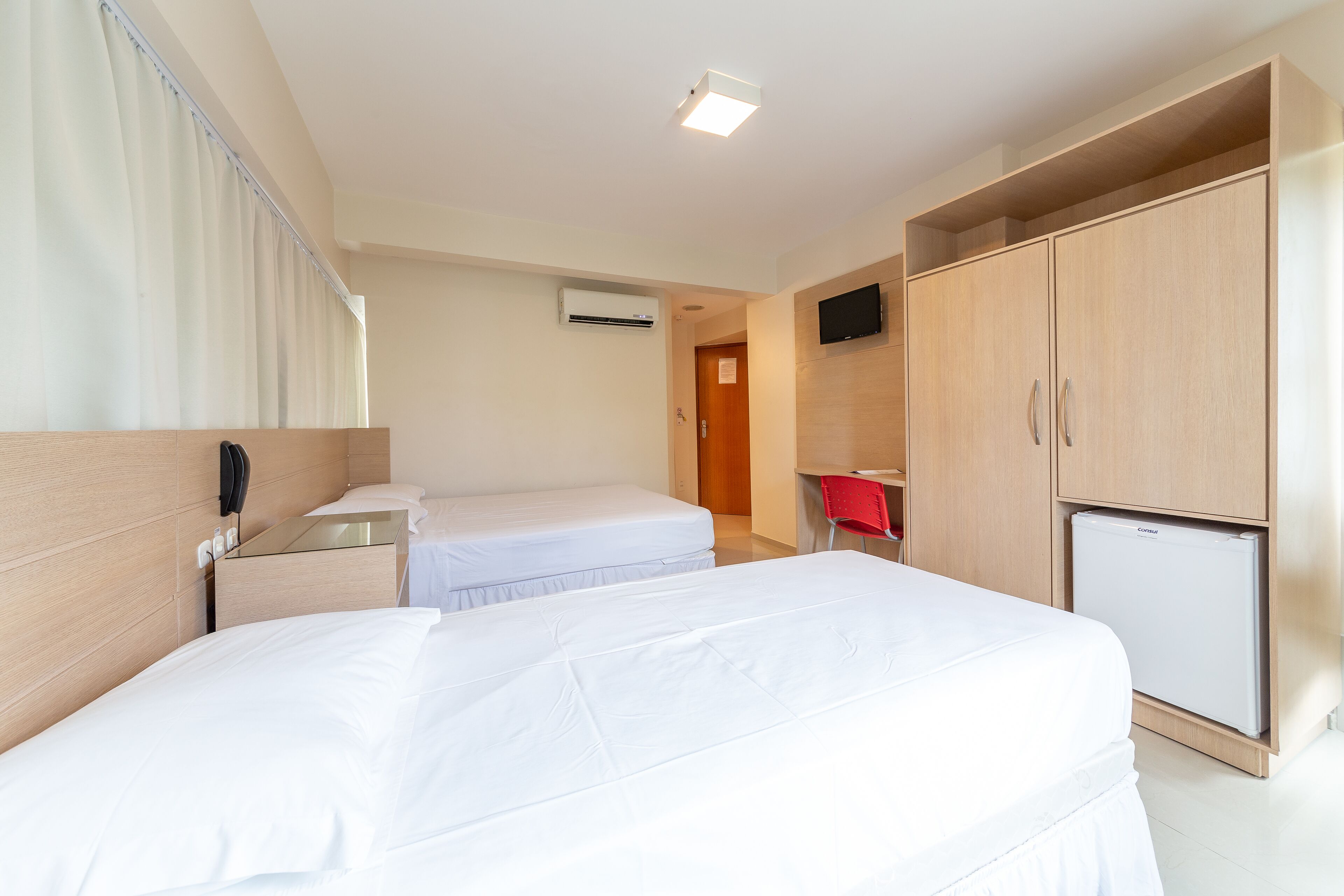 Quarto de hotel com duas camas, uma escrivaninha, uma televisão e um mini-frigorífico.