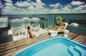 Uma área de piscina no terraço com deck de madeira, espreguiçadeiras e guarda-sóis.