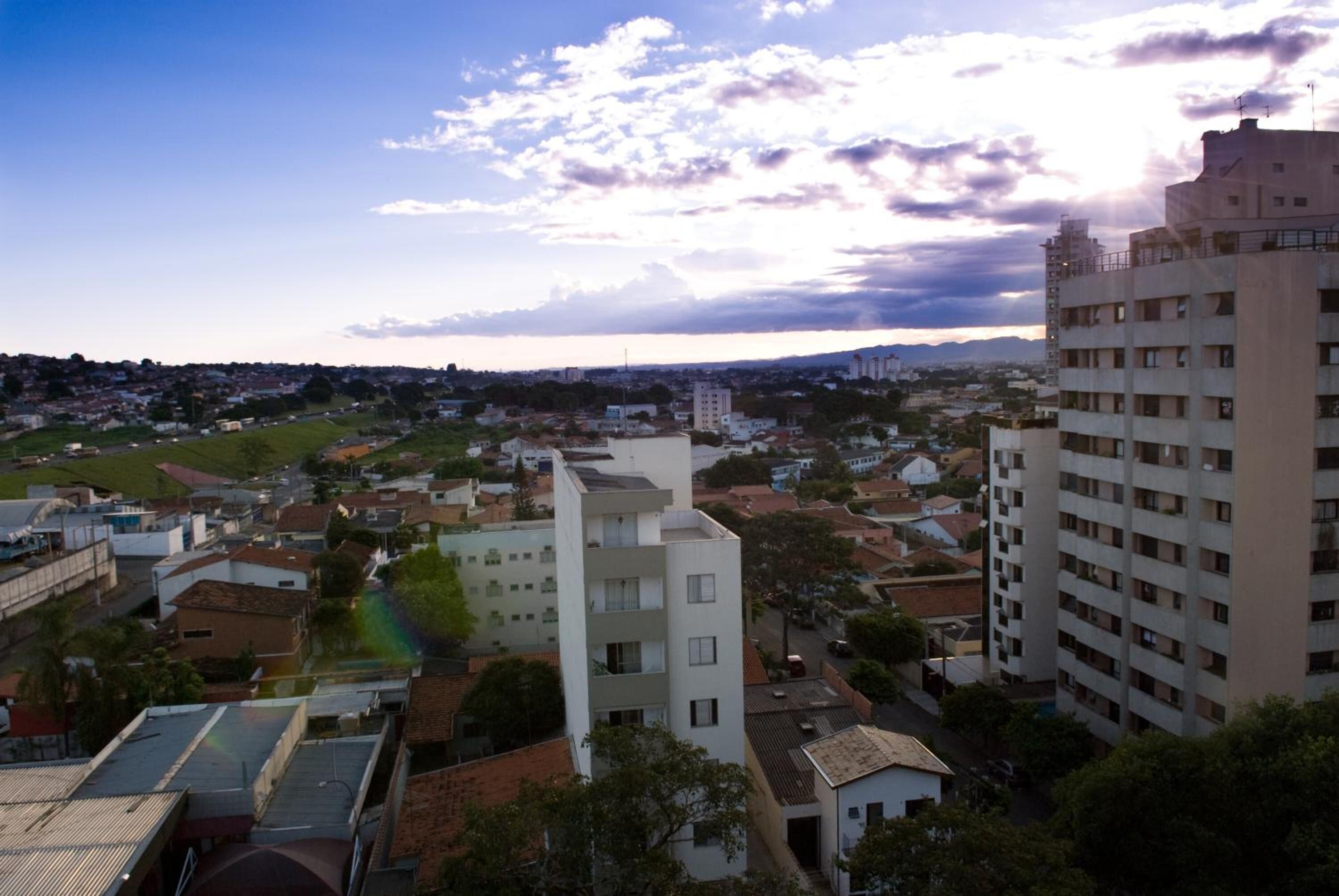 Paisagem urbana com mistura de edifícios residenciais e arranha-céus, céu claro e uma cordilheira ao longe.