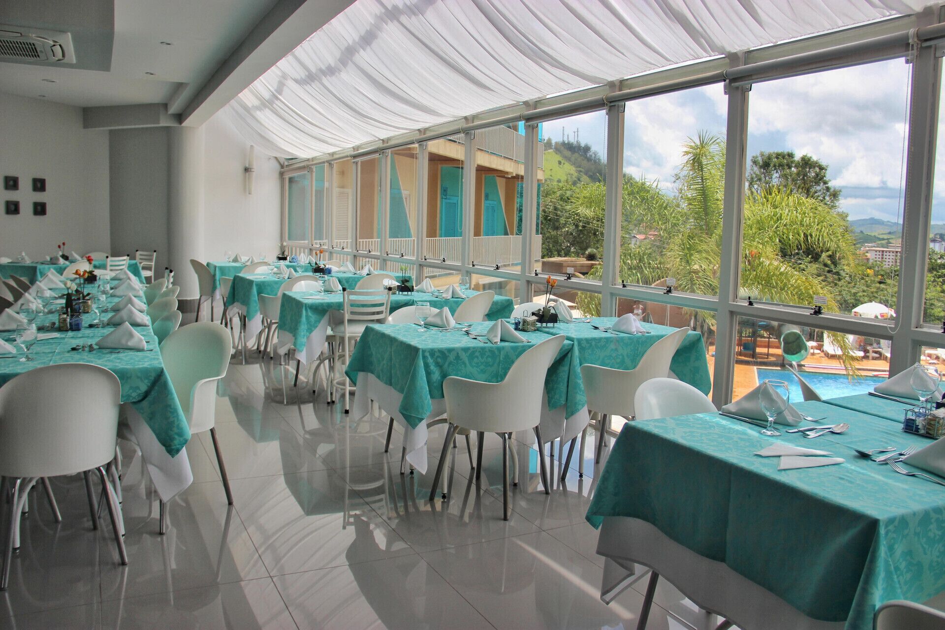 Uma sala de banquetes com fileiras de mesas, cadeiras e uma grande janela com vista para uma piscina e áreas verdes.